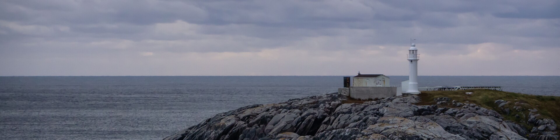 Um farol numa formação rochosa à beira-mar, sob um céu nublado.