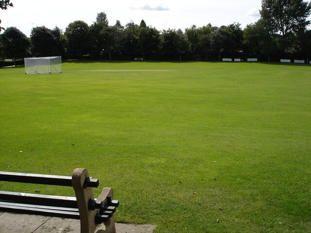 Um amplo campo verde com um gol e um banco em primeiro plano.