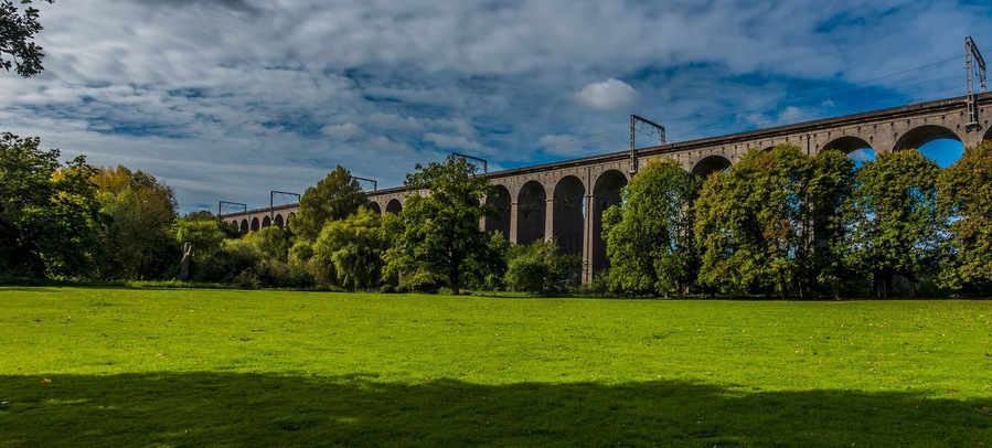 Um viaduto de pedra com várias arcos, rodeado por relva verde exuberante e árvores.