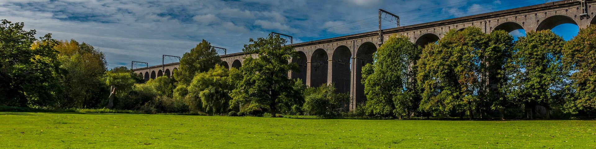 Um viaduto de pedra com várias arcos, rodeado por relva verde exuberante e árvores.