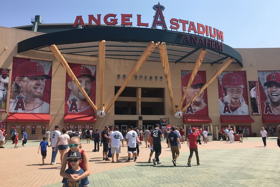 A entrada do Angel Stadium of Anaheim, com grandes banners e uma multidão de pessoas.