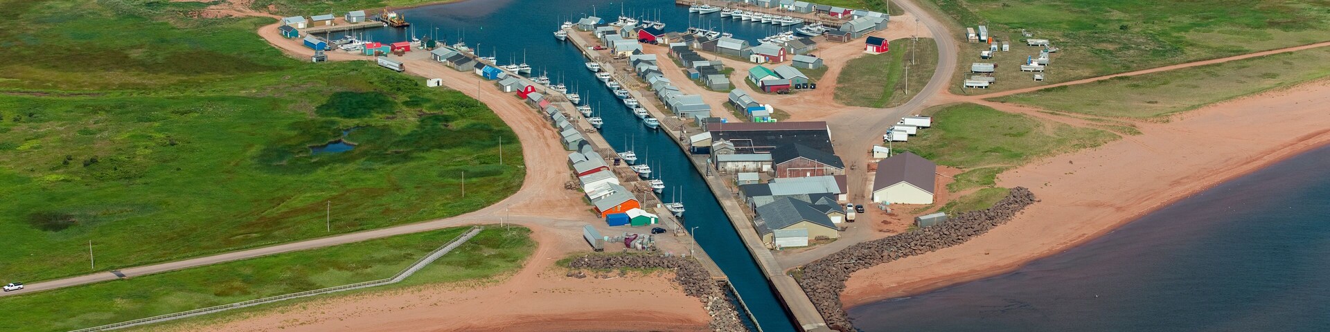 Vista aérea de uma cidade costeira com um porto de iates, barcos e um longo cais que se estende sobre a água.
