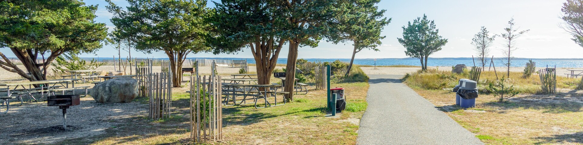 Um caminho pavimentado, mesas para piquenique e vista para o oceano.