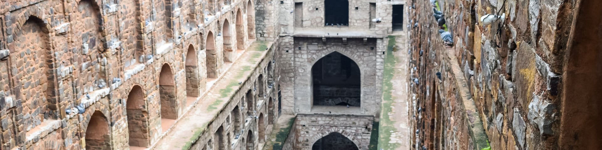 Um edifício antigo de pedra com corredores em arco e um pátio central.
