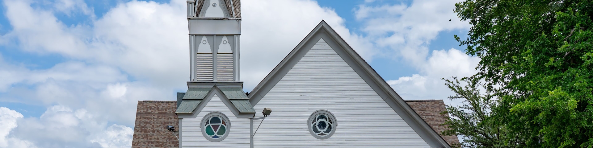 Uma igreja branca com um campanário, uma porta azul e uma pequena árvore em frente.