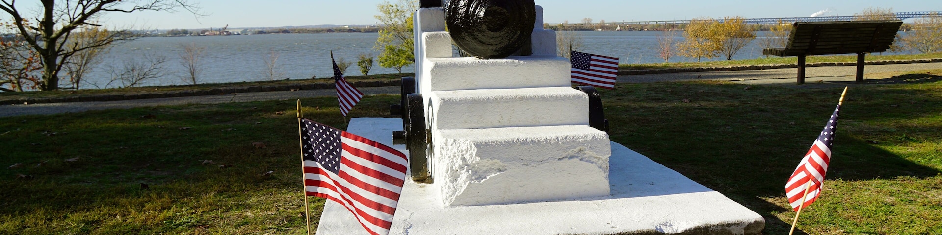 Um monumento com um canhão, cercado por grama e duas bandeiras americanas.