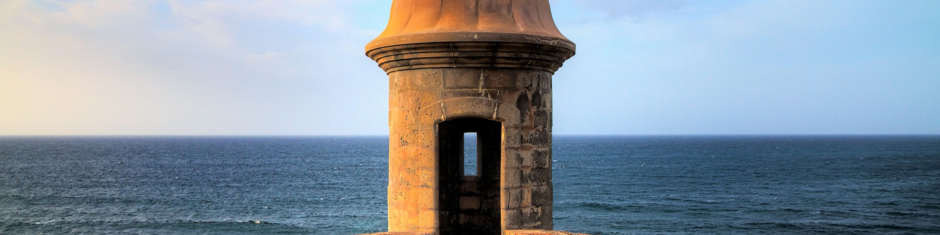 Uma fortaleza costeira com teto abobadado, uma passagem estreita e o oceano ao fundo.