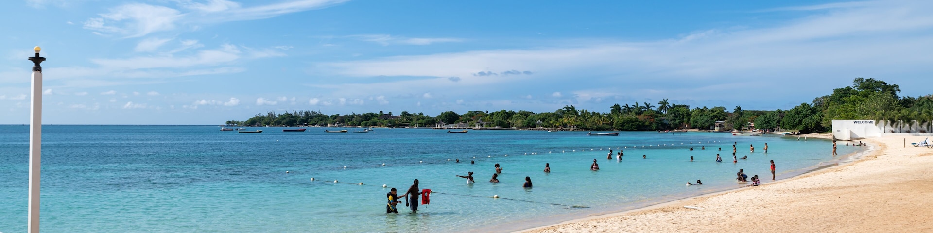 Uma praia com águas turquesa cristalinas, areal arenoso e uma ilha distante coberta de vegetação.