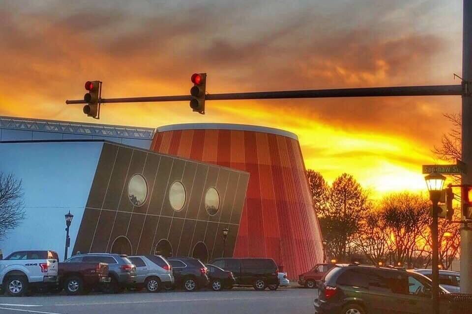 Um pôr do sol com um edifício cilíndrico grande e um semáforo.