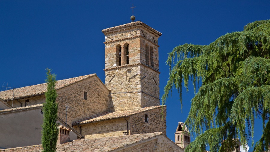 Uma igreja de pedra com uma torre de sino, telhado de telhas e um salgueiro chorão.