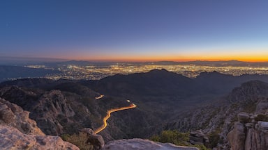 Paisagem montanhosa com uma estrada sinuosa e uma cidade iluminada ao longe.