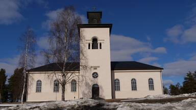 Uma igreja com uma torre alta e janelas em arco, rodeada por neve e árvores.