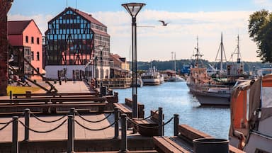 Um porto com barcos, um cais de madeira e edifícios à beira-mar.