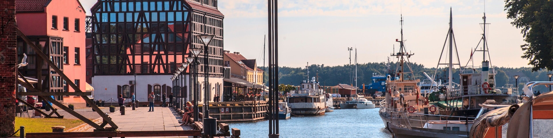 Um porto com barcos, um cais de madeira e edifícios à beira-mar.