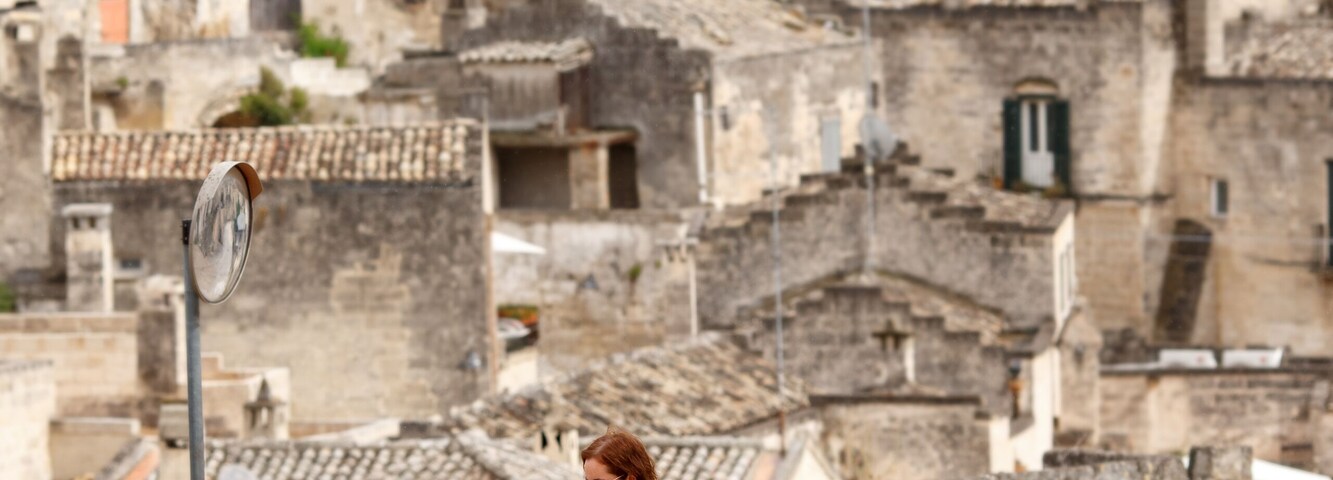 Uma antiga trilha de pedra, com uma mulher e uma criança em primeiro plano e uma encosta densamente povoada por edifícios antigos ao fundo.