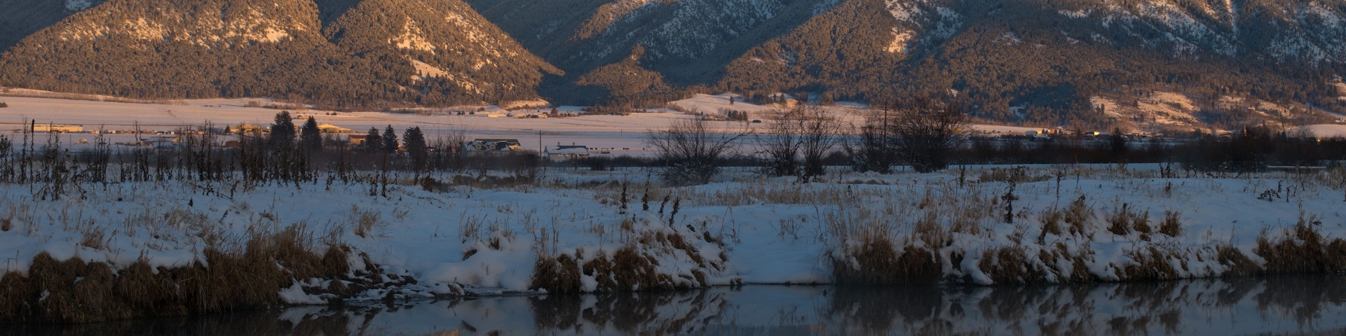 Paisagem coberta de neve com um lago calmo refletindo montanhas e céu.