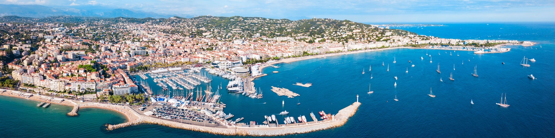 Paisagem costeira com um porto, barcos e um horizonte montanhoso.