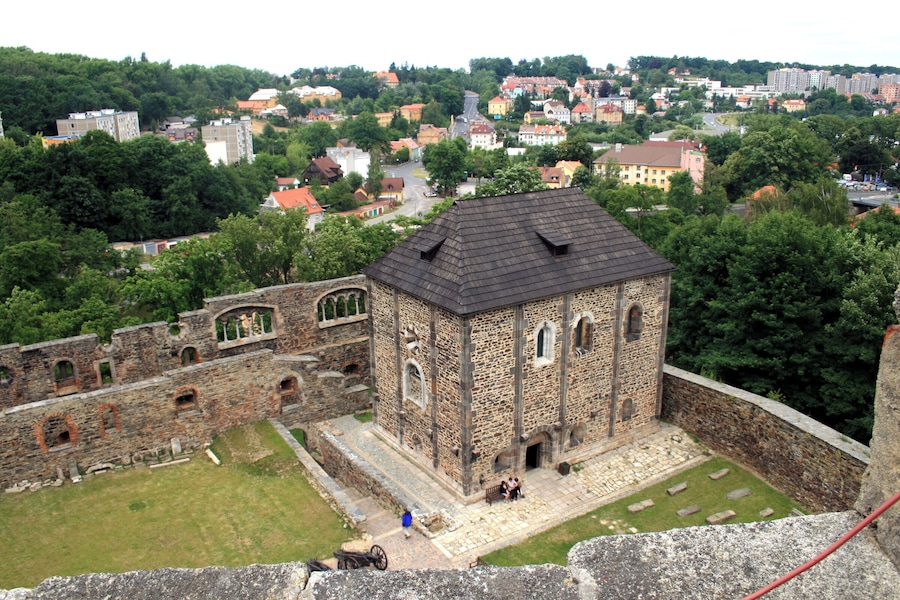 Um edifício histórico de pedra com telhado em telhas, rodeado por um relvado bem cuidado e um fosso.