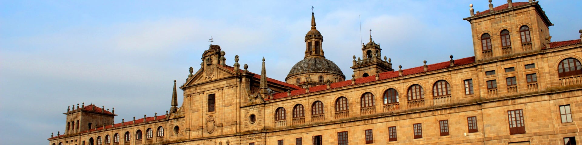 Um grande edifício histórico com várias cúpulas e torres, um pátio e um céu azul límpido.