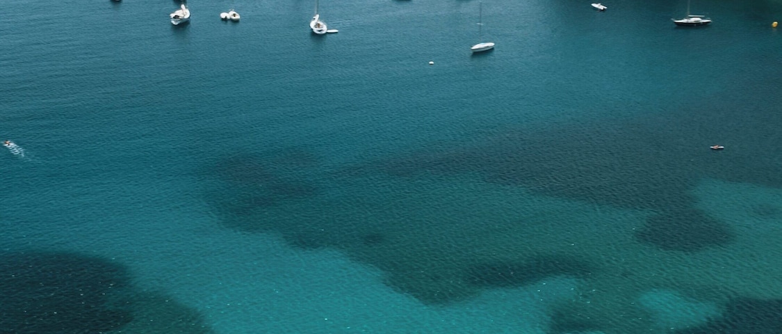 Uma cidade costeira com águas turquesa cristalinas, um porto cheio de barcos e uma praia com pessoas.