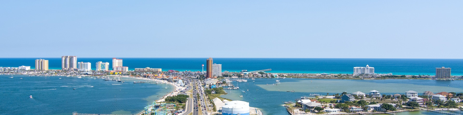 Paisagem costeira urbana com uma ponte imponente, marina e edifícios altos ao longo da orla.