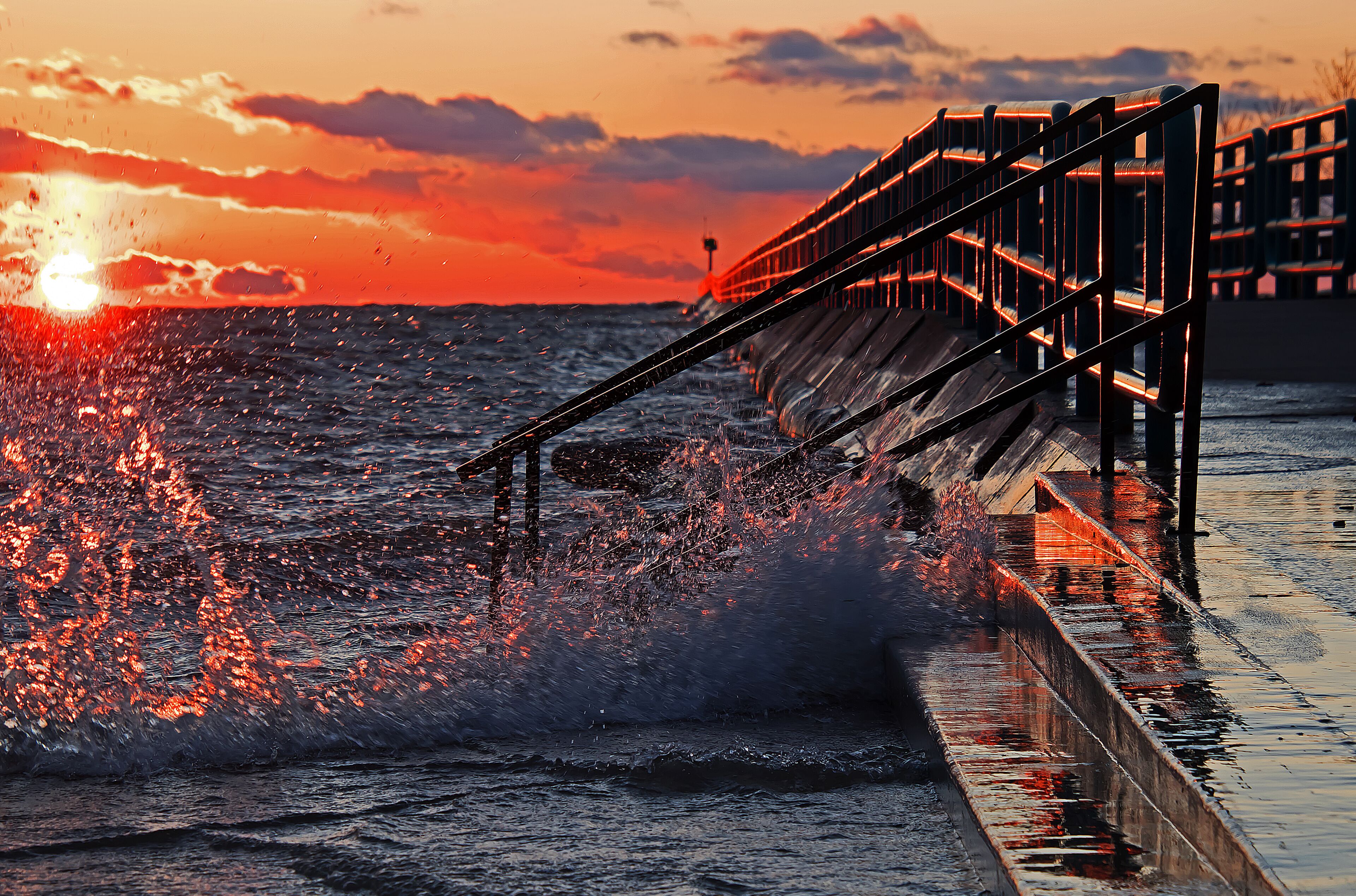 Um cais se estendendo para o oceano ao pôr do sol, com ondas batendo contra ele.