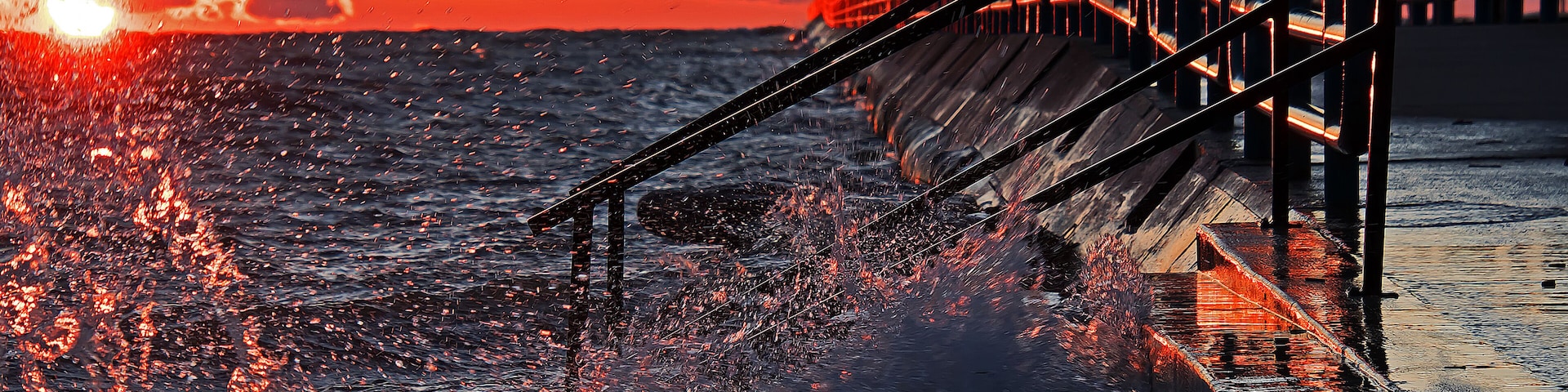 Um cais se estendendo para o oceano ao pôr do sol, com ondas batendo contra ele.