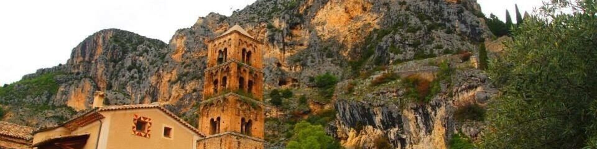 Uma aldeia com uma igreja imponente e uma montanha rochosa ao fundo.