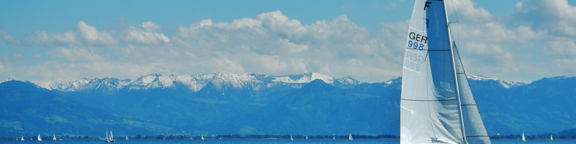 Um veleiro com vela branca em um lago, com montanhas ao fundo.