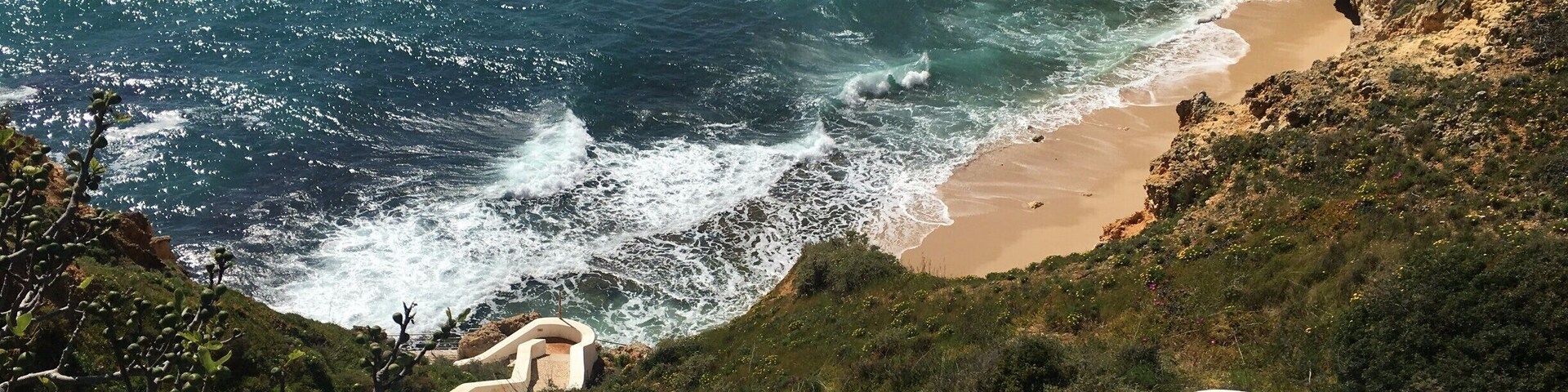 Paisagem costeira com um caminho sinuoso, falésias rochosas e uma praia.