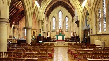 Interior de igreja com tetos abobadados, bancos de madeira e vitrais.