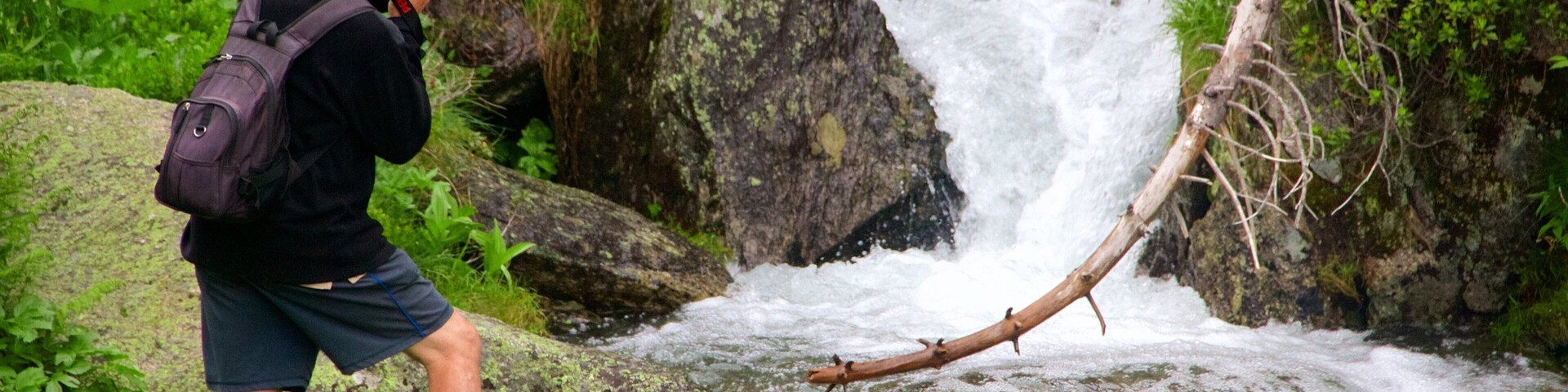 Um caminhante observando uma cascata cercada por vegetação exuberante e pedras.