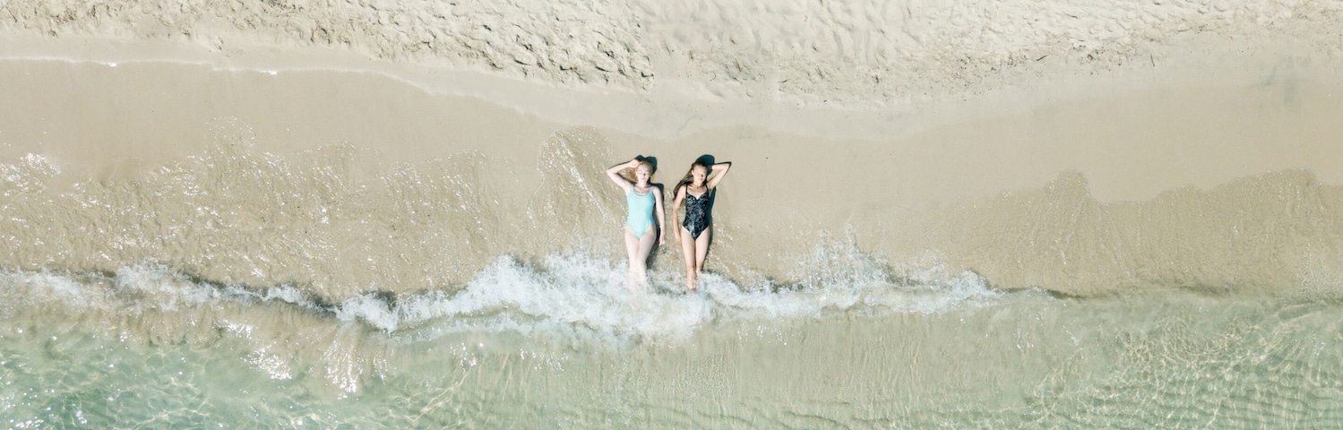 Uma praia com água cristalina, pessoas de fato de banho e guarda-sóis coloridos.
