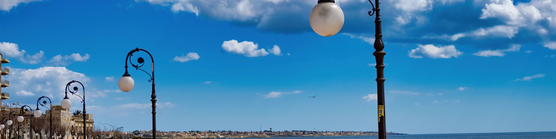 Um calçadão à beira-mar com céu claro, praia arenosa e mar calmo.