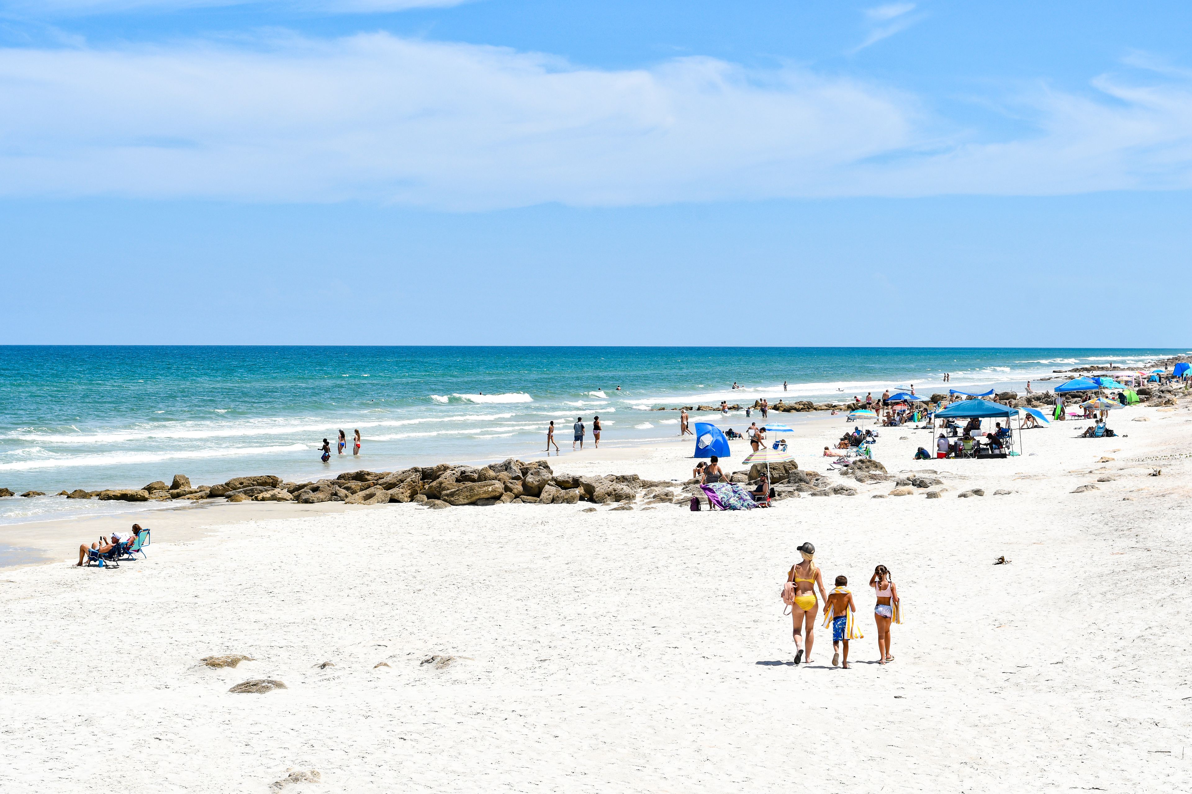 Uma praia com pessoas, guarda-sóis e rochas.