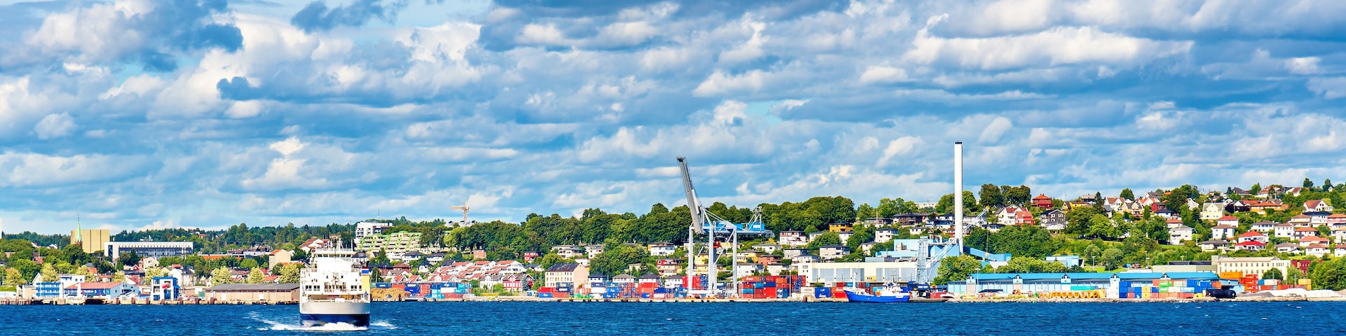 Uma cidade costeira com uma grande massa de água, um navio e guindastes industriais.