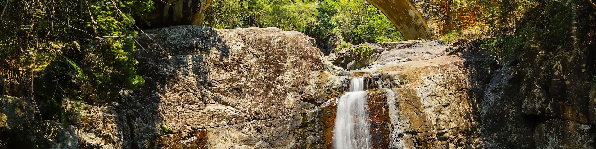 Uma ponte de pedra sobre uma cascata numa área arborizada.