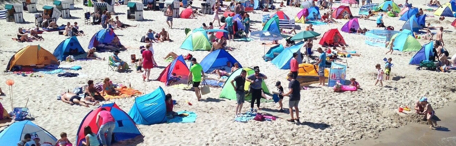 Praia movimentada com várias tendas coloridas e pessoas aproveitando o tempo ensolarado.
