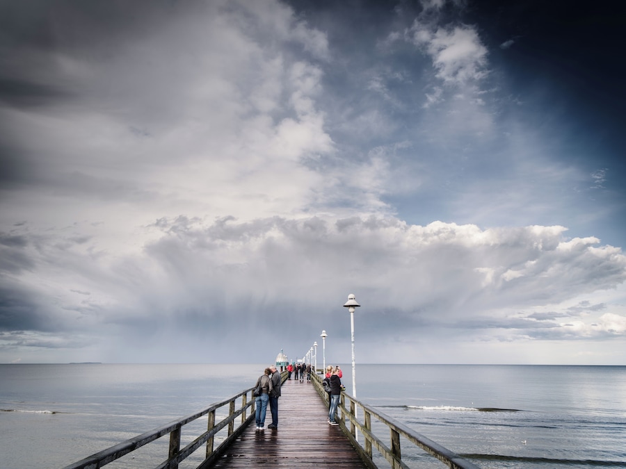 Um píer de madeira que se estende até o mar, com pessoas caminhando.
