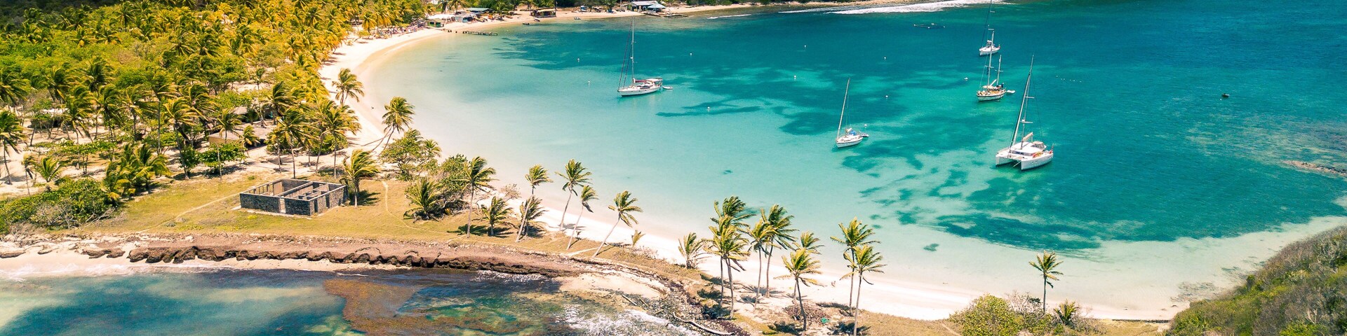 Uma praia tropical com águas turquesa cristalinas, palmeiras e uma pequena ilha ao longe.