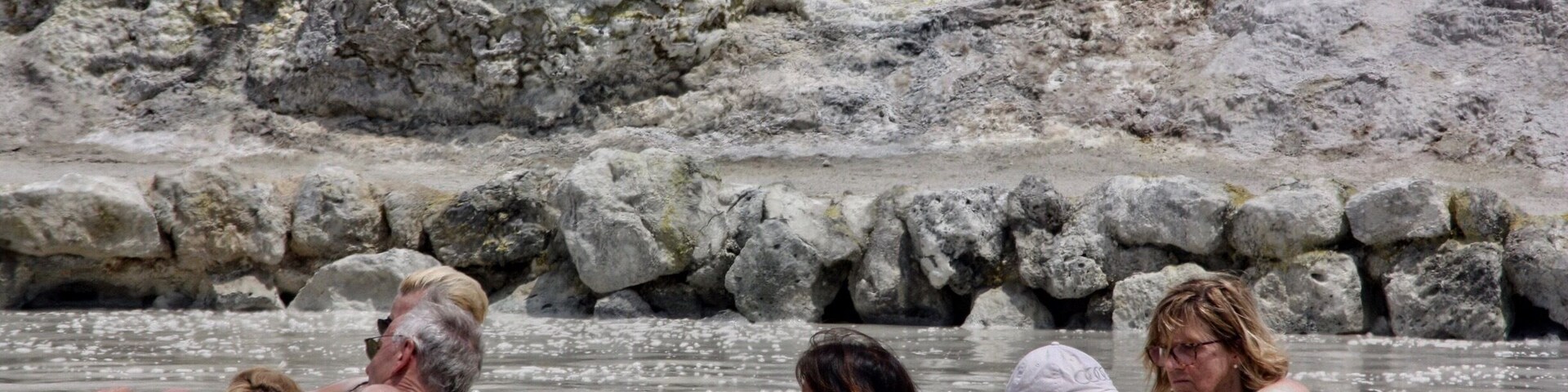 Pessoas em um spa geotérmico com água rica em minerais e terreno rochoso ao fundo.