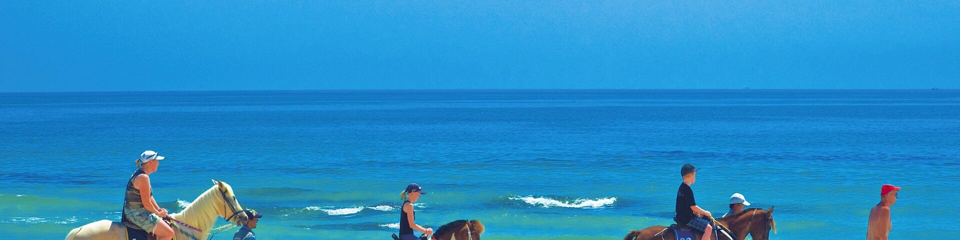 Uma praia com pessoas cavalgando cavalos ao longo da costa.