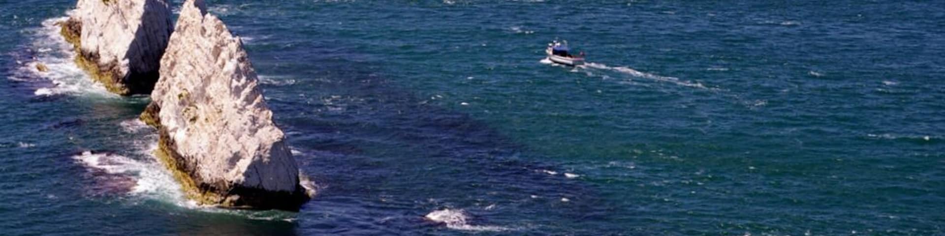 Um litoral rochoso com um farol e um barco na água.