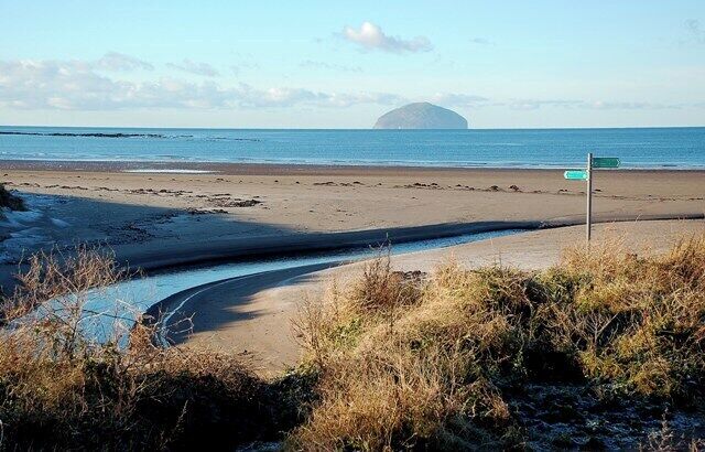 Uma praia com um sinalizador, um pequeno riacho e uma ilha ao longe.