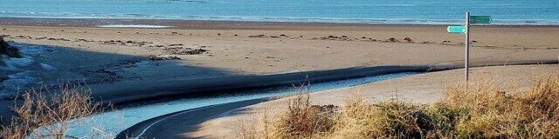 Uma praia com um sinalizador, um pequeno riacho e uma ilha ao longe.