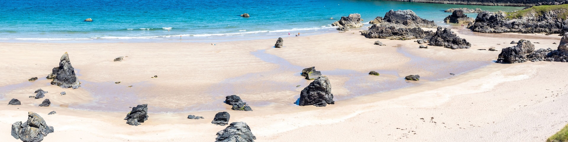 Uma praia de areia com pedras espalhadas e mar azul cristalino.
