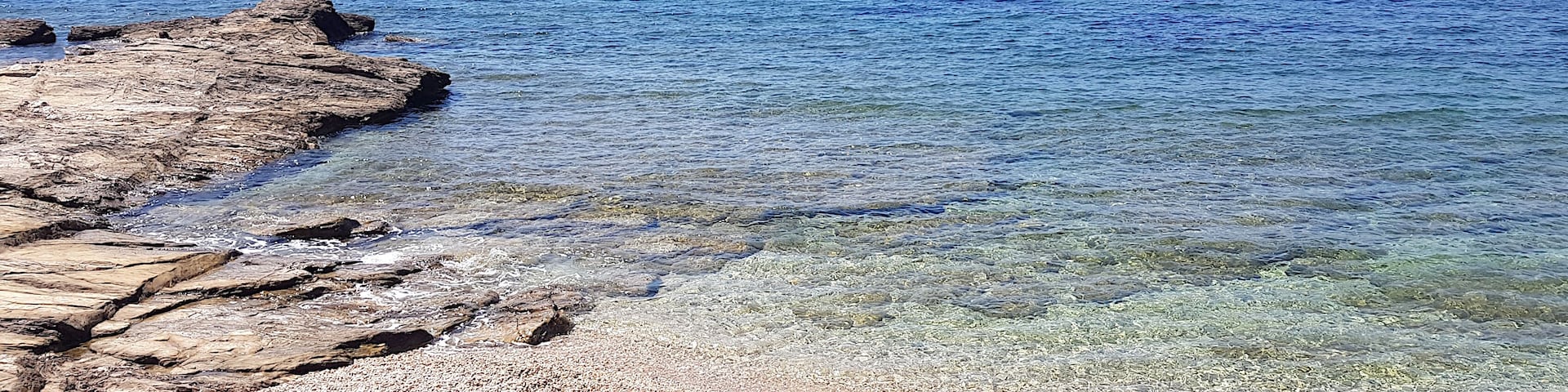 Litoral rochoso com águas cristalinas e um barco ao longe.