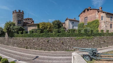 Uma rua de paralelepípedos, uma torre de pedra histórica e um edifício com fachada de tijolos.