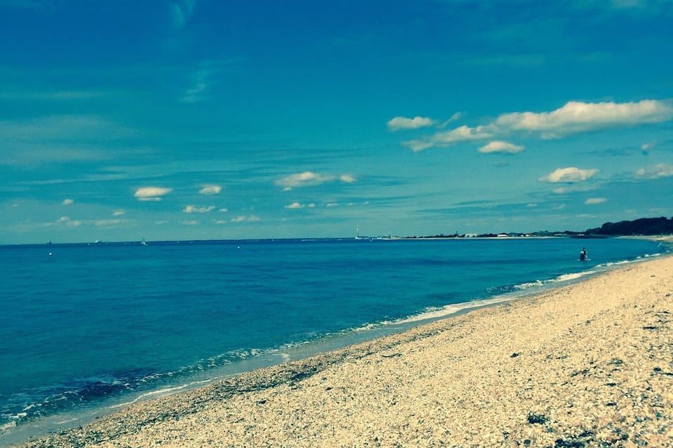 Uma praia de pedras com céu azul límpido e mar calmo.