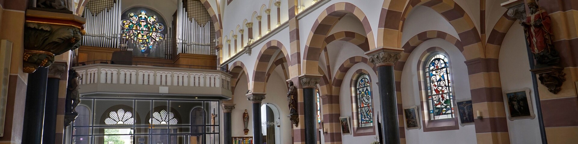 Interior de igreja com tetos arqueados, vitrais e bancos de madeira.